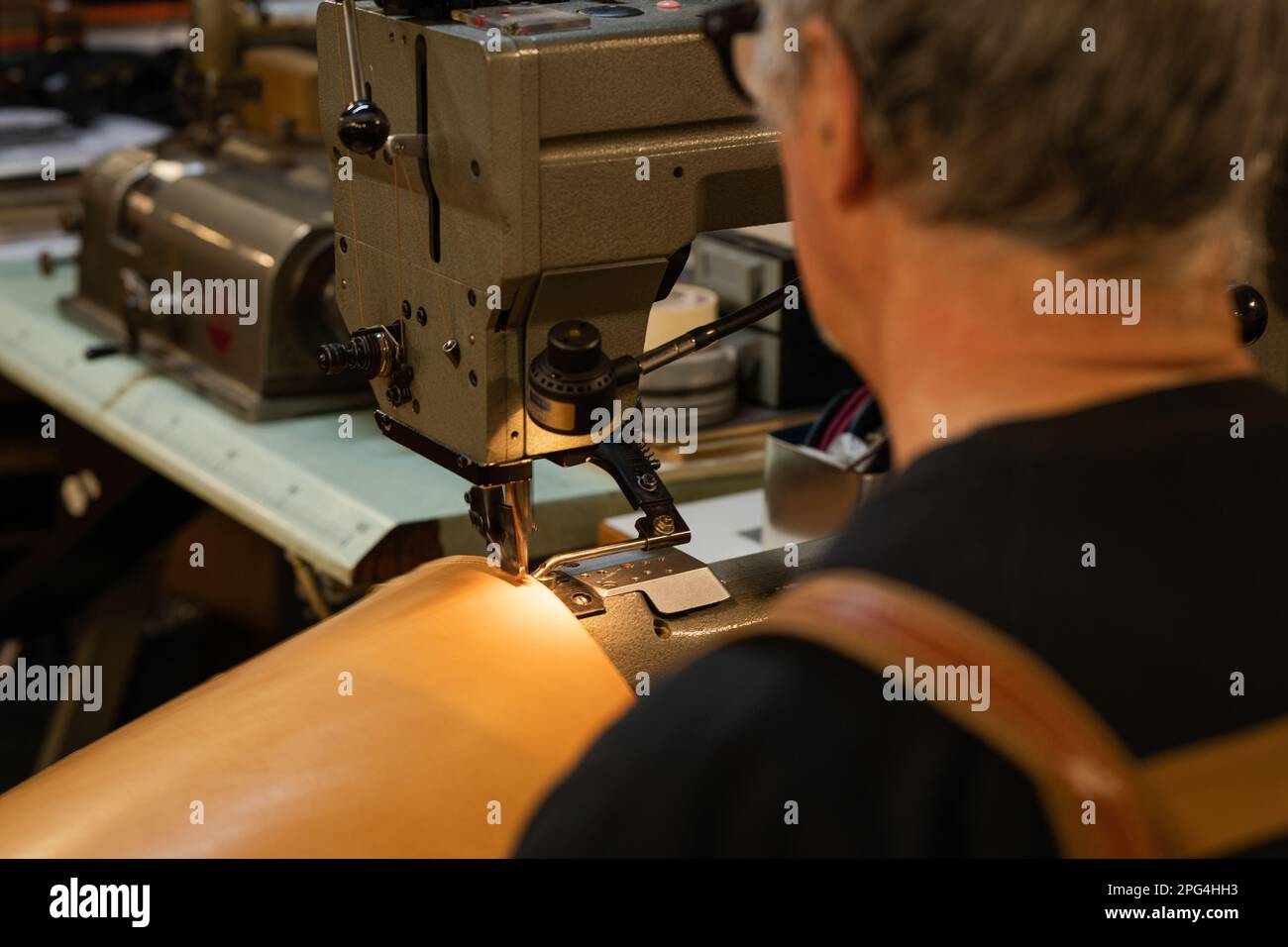 Close-up of sewing machine with a leather craftsman sitting behind ...