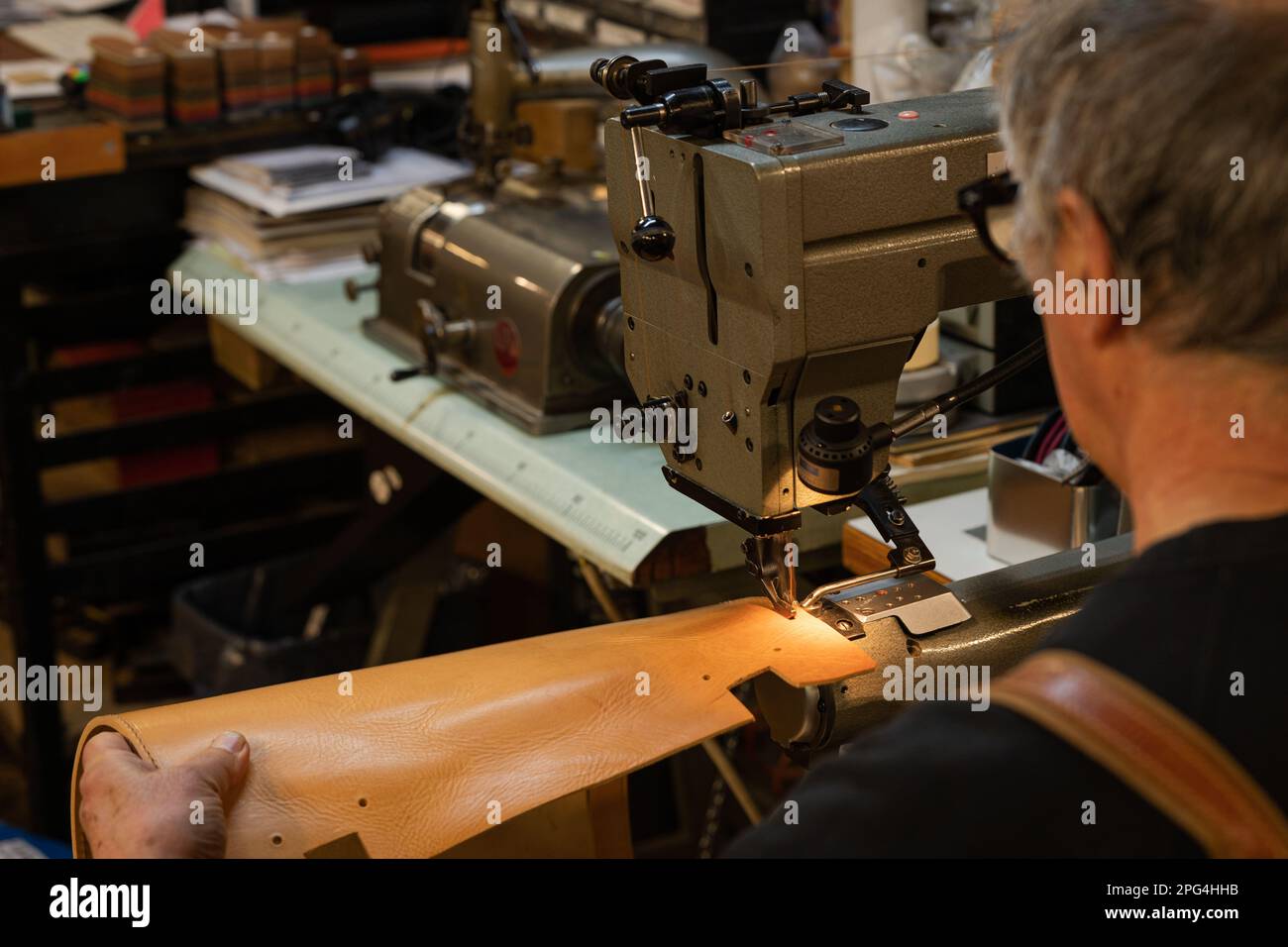 view of a leather craftsman’s shoulders sitting while sewing a leather ...