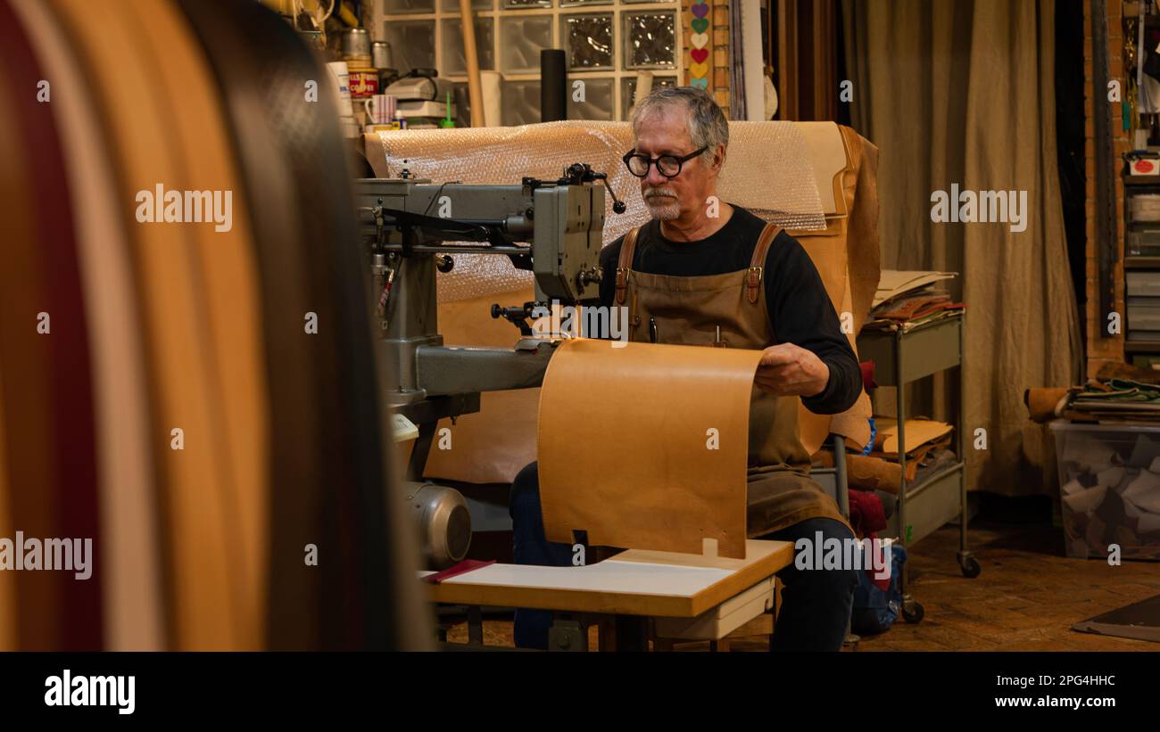 senior tanner sitting sewing leather back panel with a sewing machine ...