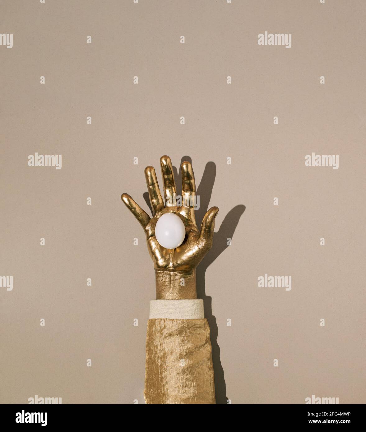 Gold painted hand holding white painted egg agains grey background ...