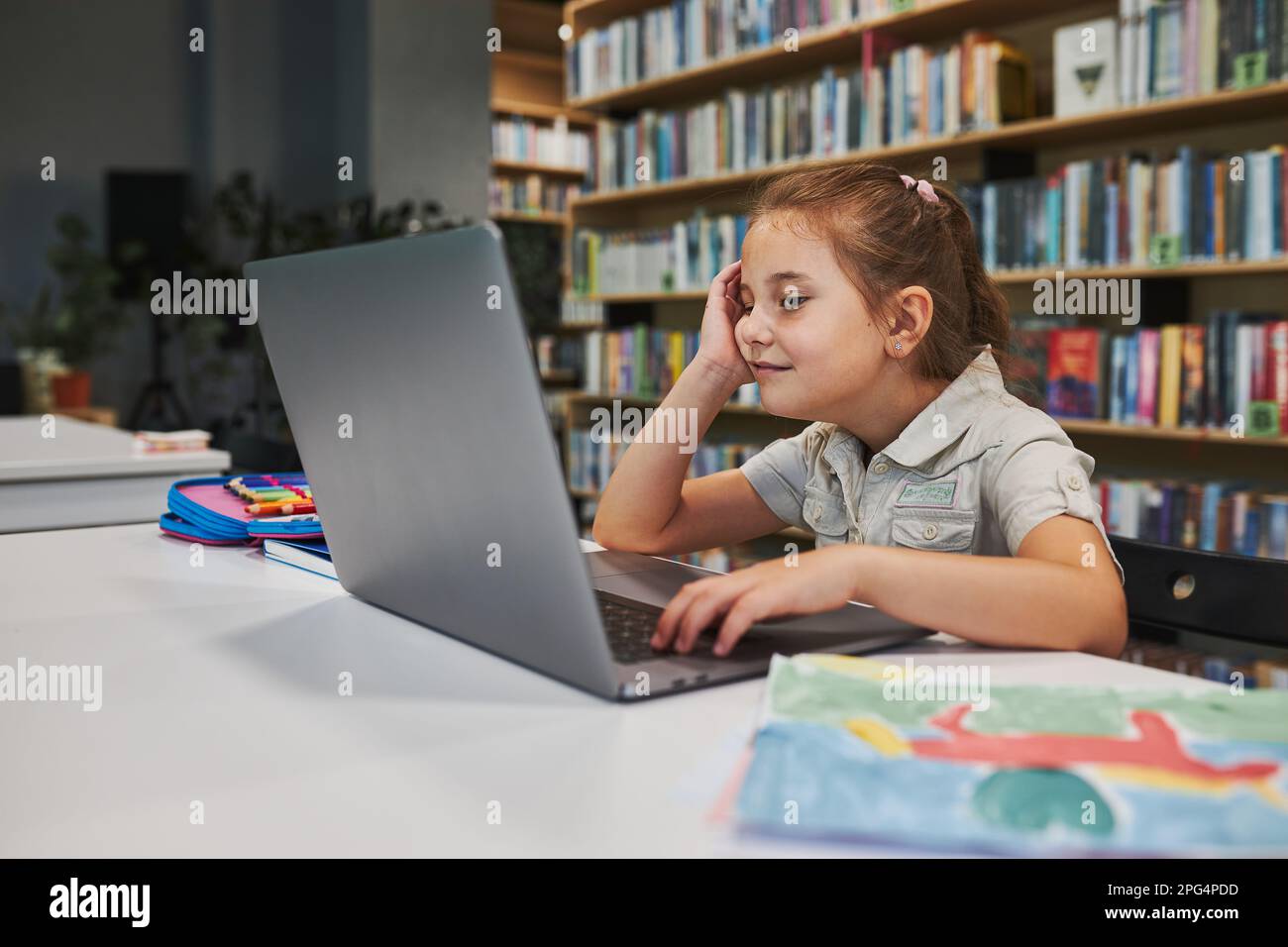 Positively engaged student doing her homework using laptop in after ...