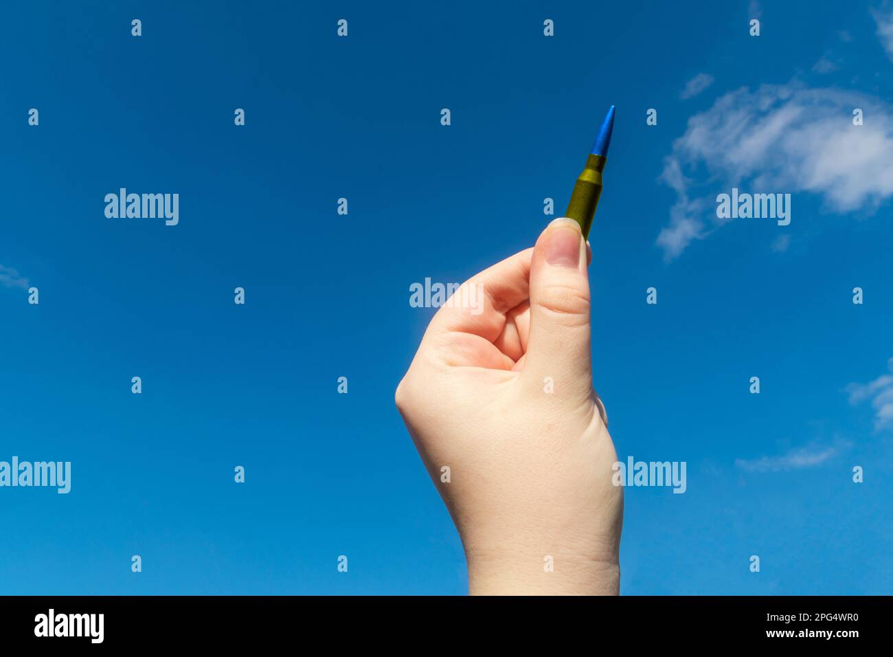 Yellow-blue rifle cartridge in hand against the blue sky (national ...