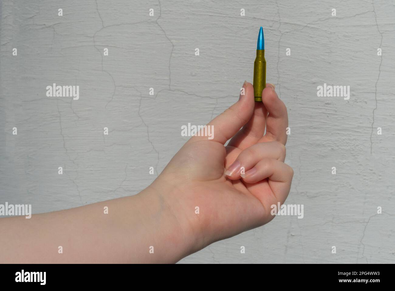 A yellow-blue rifle cartridge in a hand against a white wall (national ...