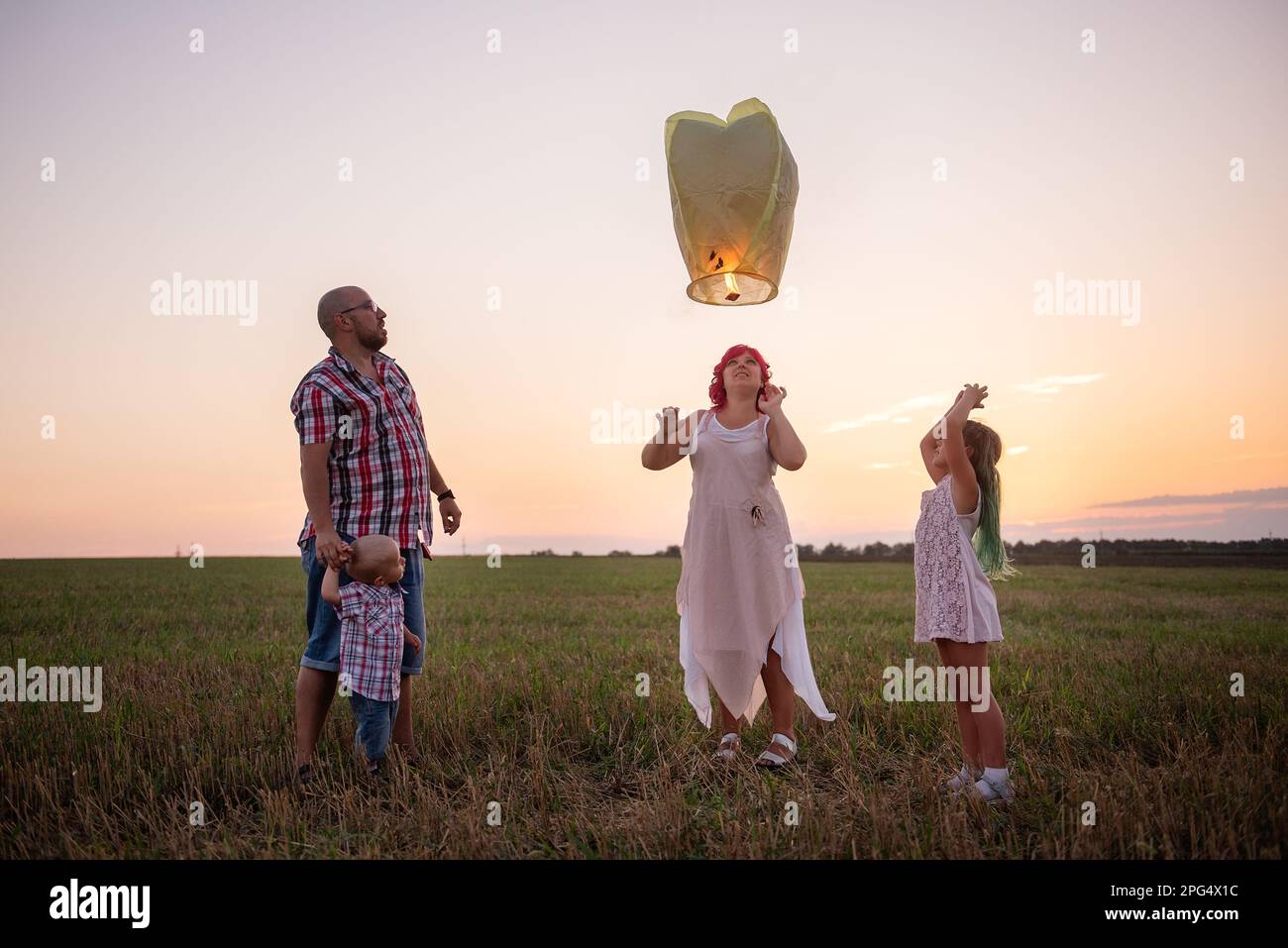 Diversity family launch yellow sky lantern in field at sunset. Mother ...