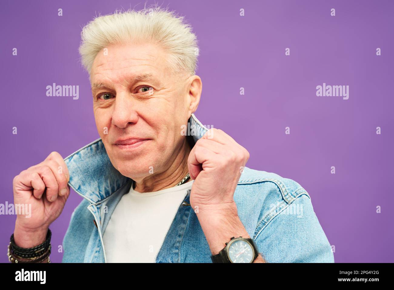 Senior man in stylish denim jacket holding edges of collar and looking ...