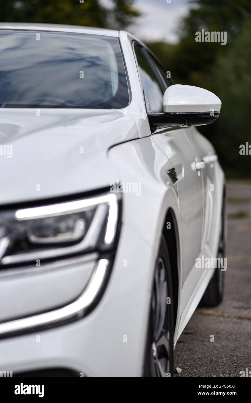 A vertical closeup detail of a white automobile parked in a green ...
