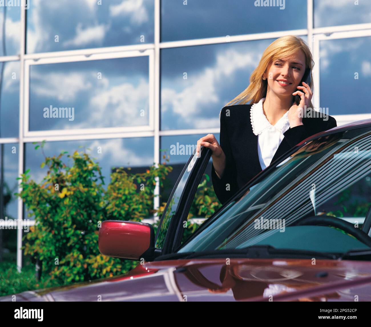 Businesswoman with cell phone standing by a vintage BMW car outside ...
