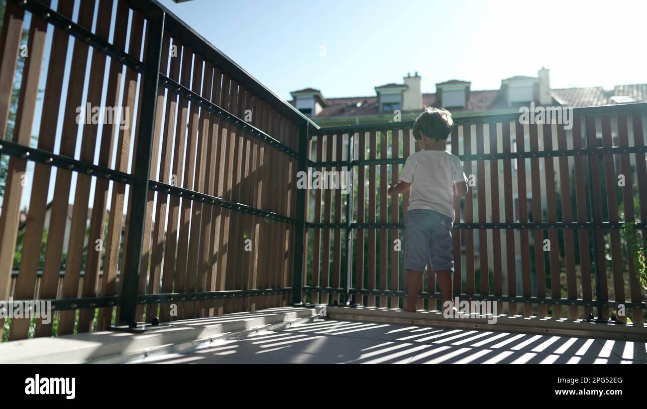 One small boy standing by balcony fence staring outside from second ...