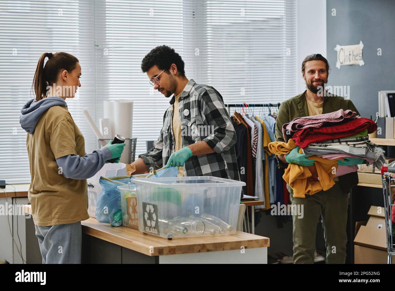 Two young volunteers sorting garbage while man carrying stack of second ...