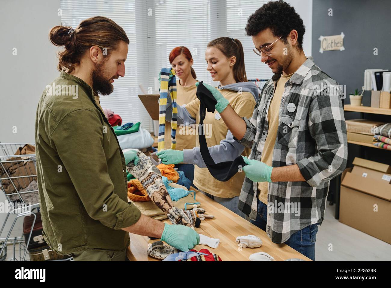 Group of four intercultural volunteers sorting second hand clothes ...