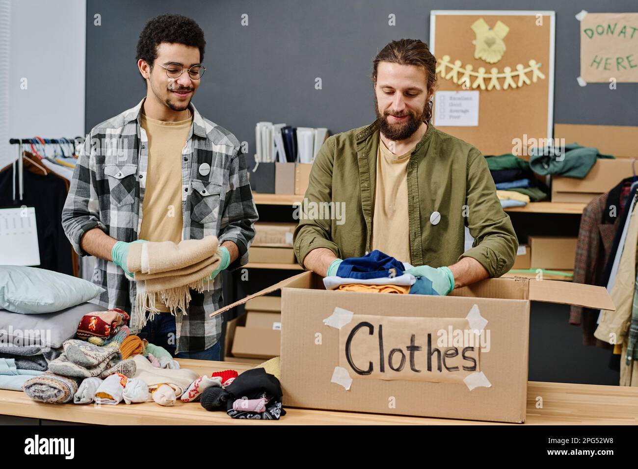 Two happy young intercultural male volunteers preparing second hand ...