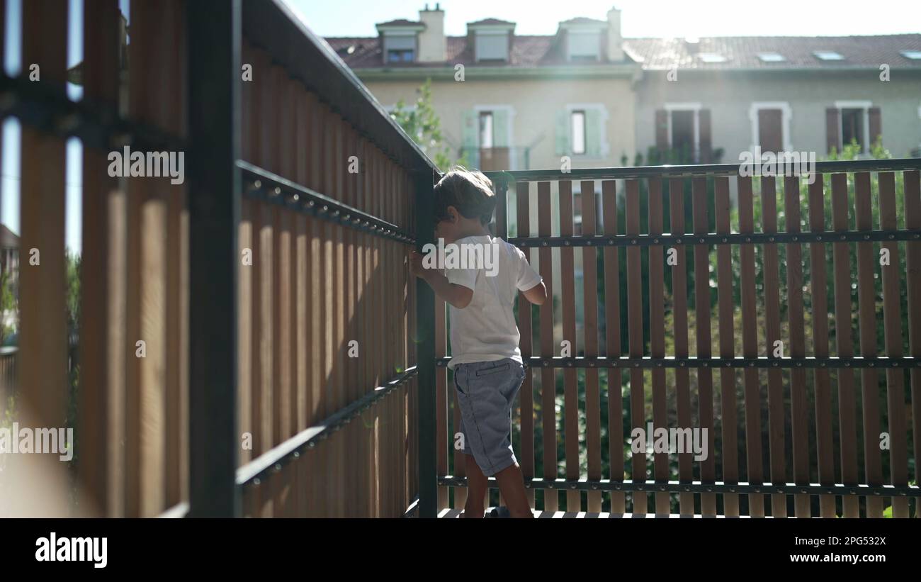 One playful child standing at apartment balcony looking through wooden ...