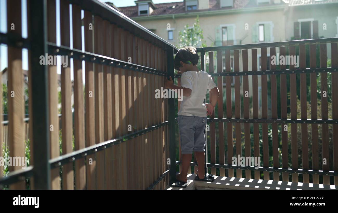 One playful child standing at apartment balcony looking through wooden ...