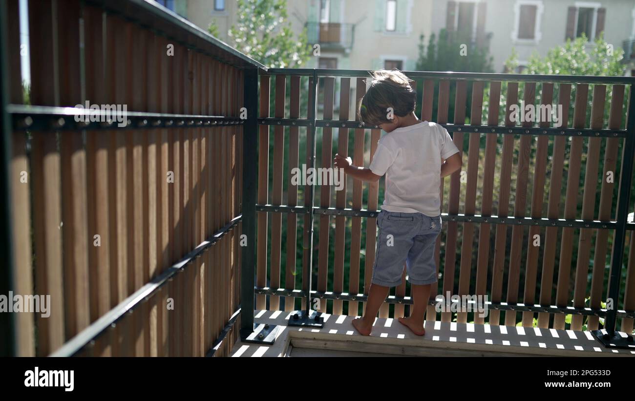 One playful little boy standing at apartment balcony in sunlight. Child ...