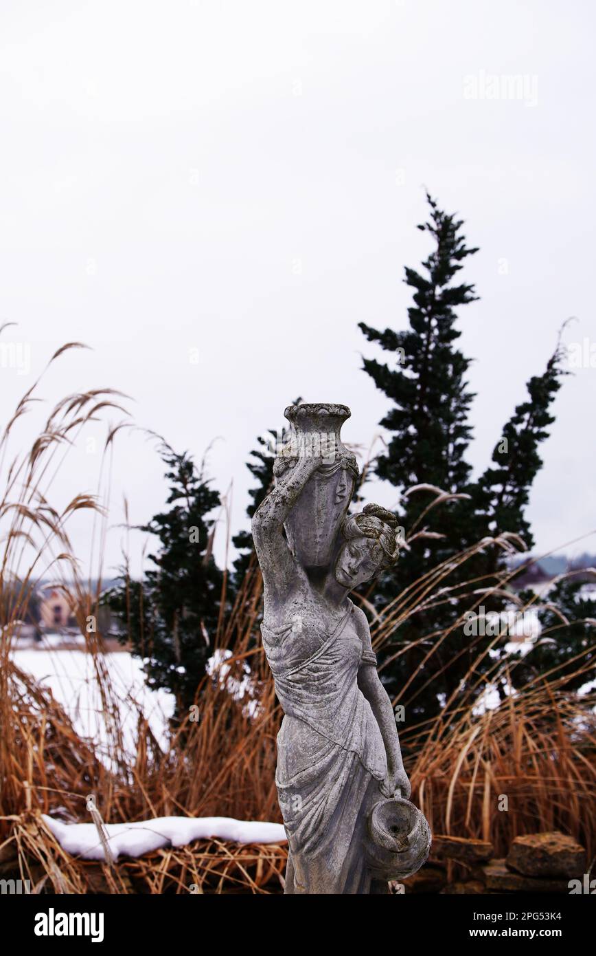 A vintage statue of an woman carrying a jug, stands alone in the middle ...