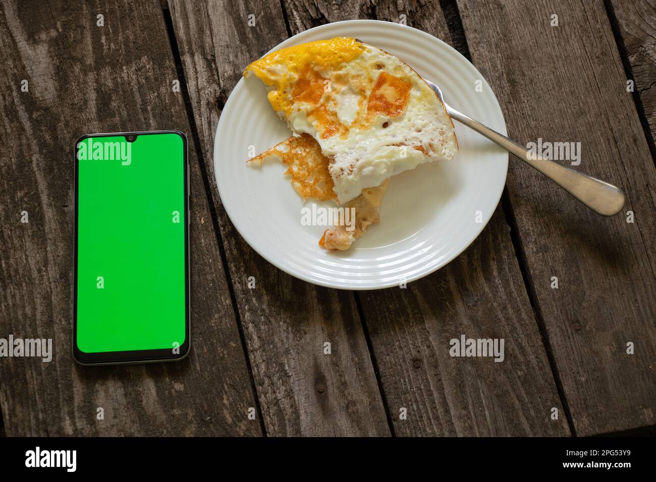 fried egg on a white plate on an wooden table and a phone with a green ...