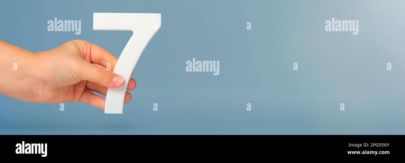 Number seven in hand. Hand holding white number 7 on blue background ...