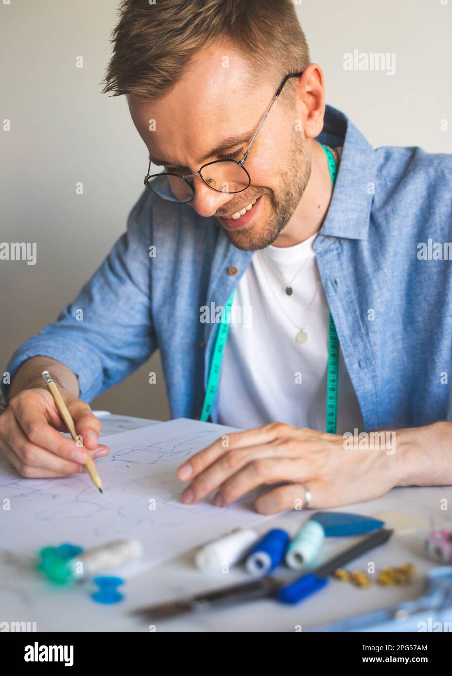 A seamster with glasses. A smiling man in a blue shirt makes a sketch ...
