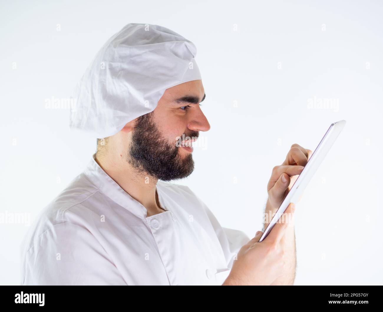 Young male chef using a tablet, reading a recipe. Isolated on a white ...