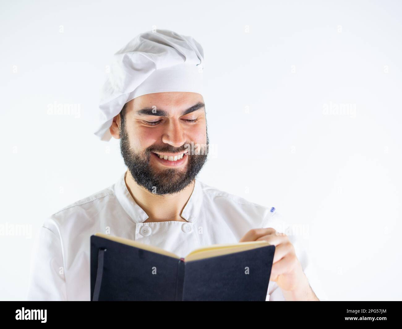 Young male chef using a notebook, writing a recipe. Isolated on a white ...