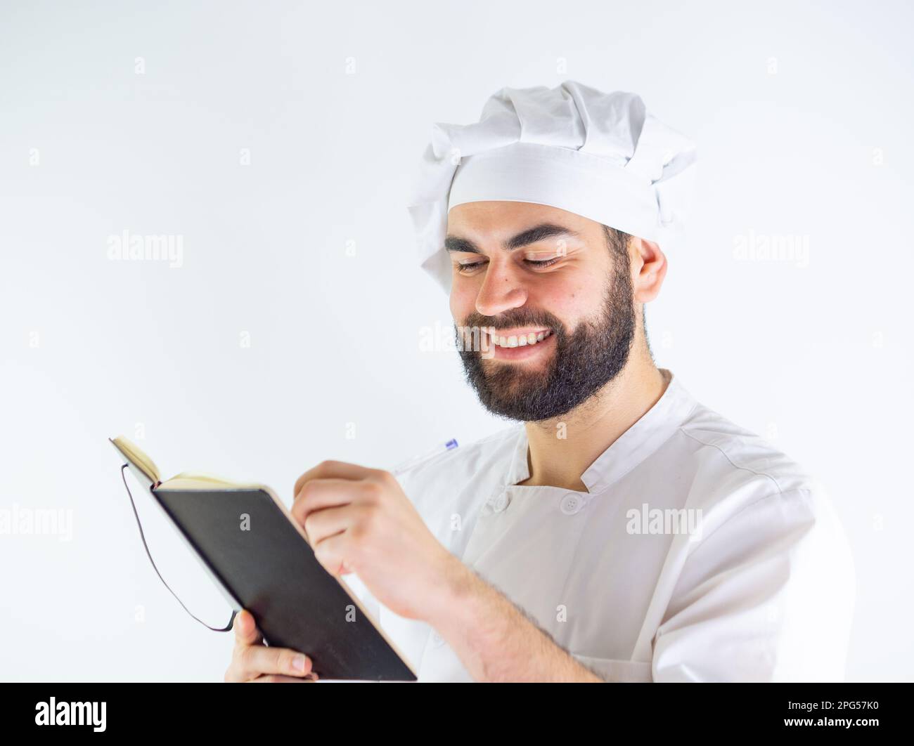 Young male chef using a notebook, writing a recipe. Isolated on a white ...