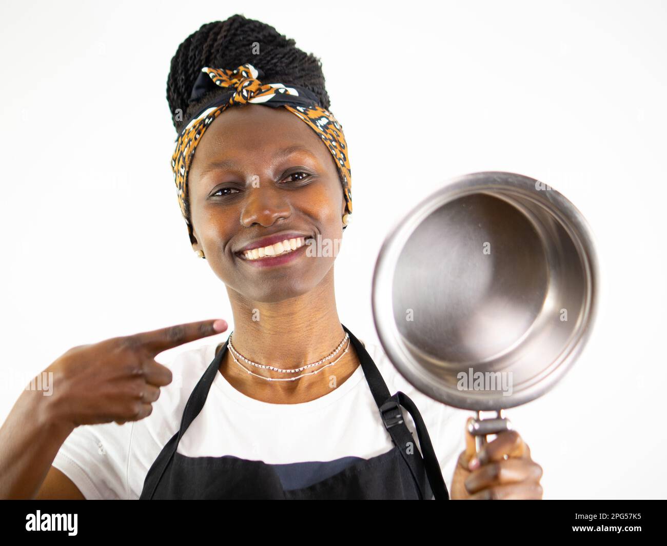 Young female chef showing and pointing a saucepan while smiling and ...