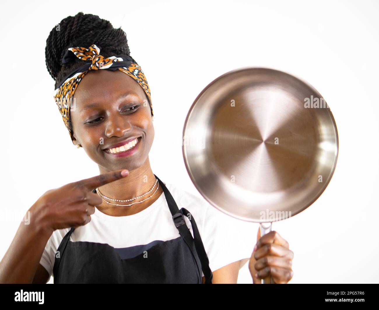 Young female chef showing and pointing a stainless pan while smiling ...