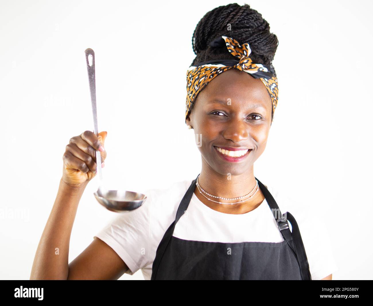 Young female chef showing a metal ladle while smiling and looking at ...