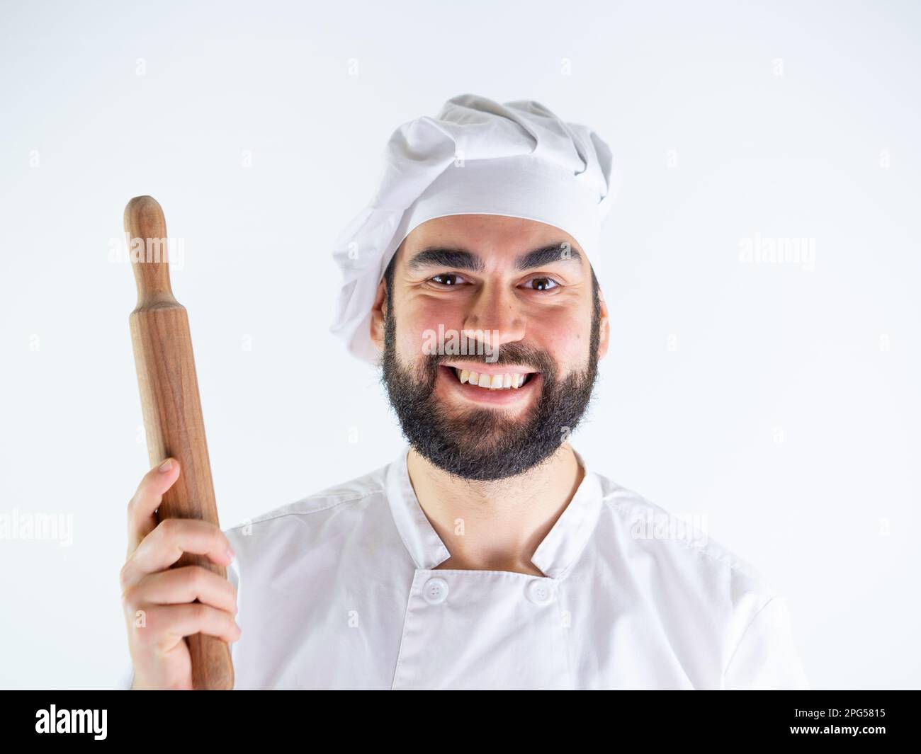 Young male chef showing a wooden rolling pin while smiling and looking ...