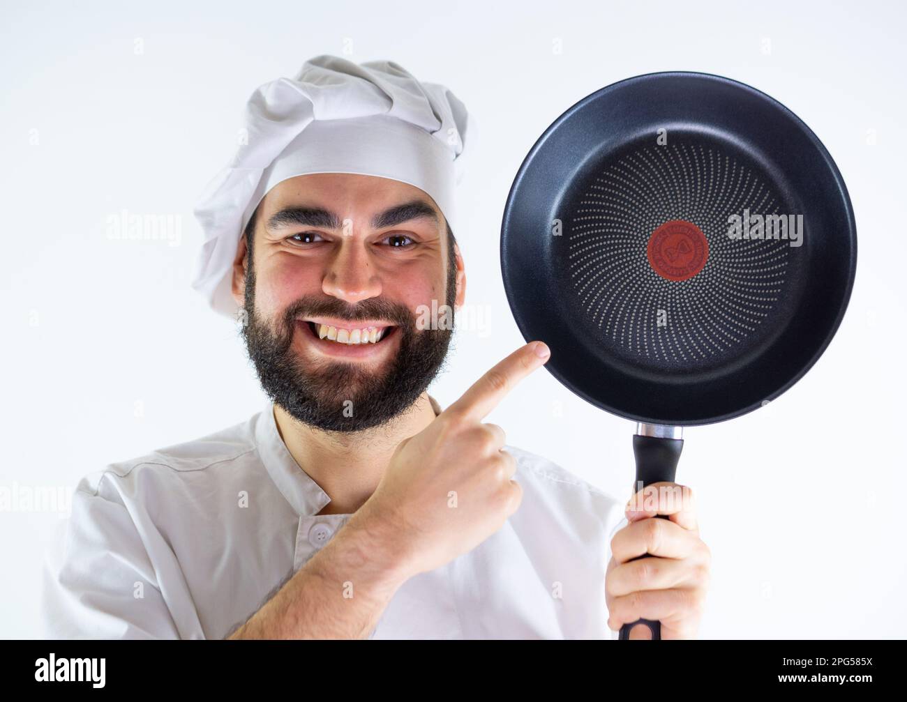 Young male chef showing a non stick pan while smiling and looking at ...