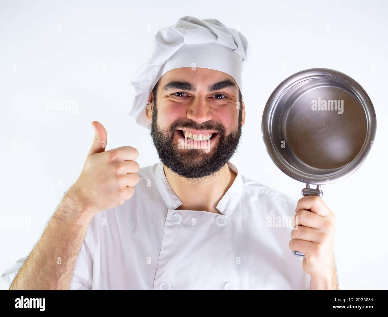 Young male chef showing a stainless saucepan while smiling and looking ...