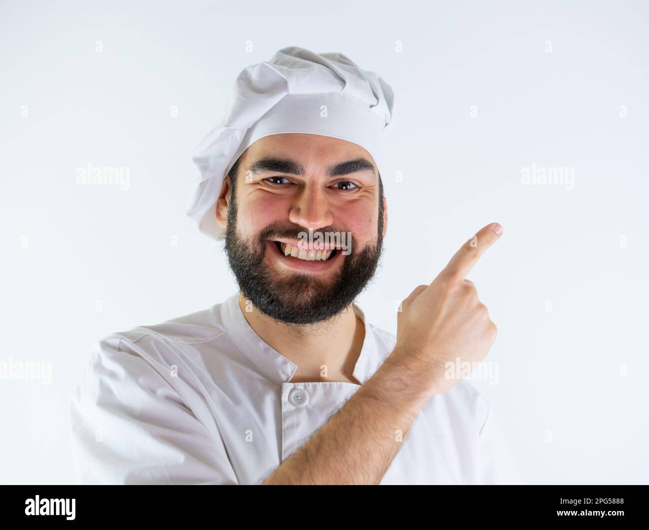 Young male chef pointing right while smiling and looking at camera ...