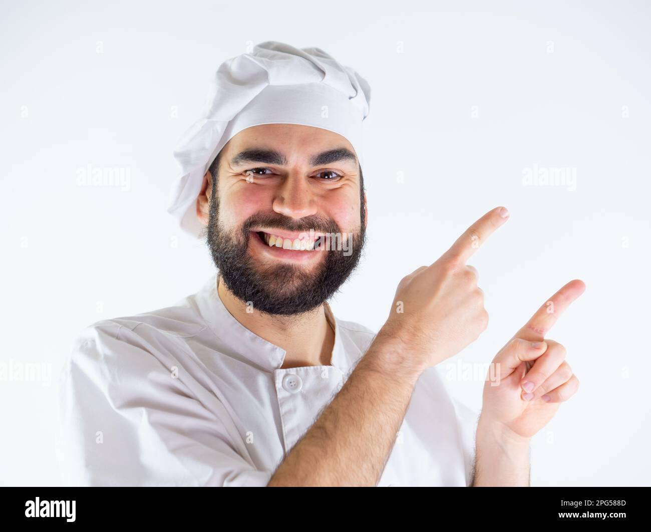 Young male chef pointing right while smiling and looking at camera ...