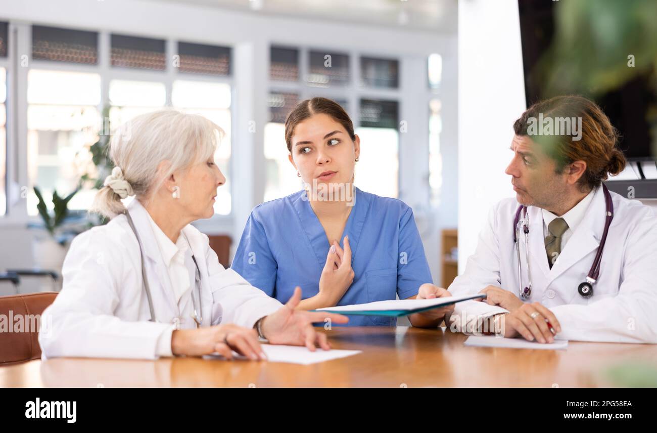 three positive doctors are sitting at table animatedly and actively ...