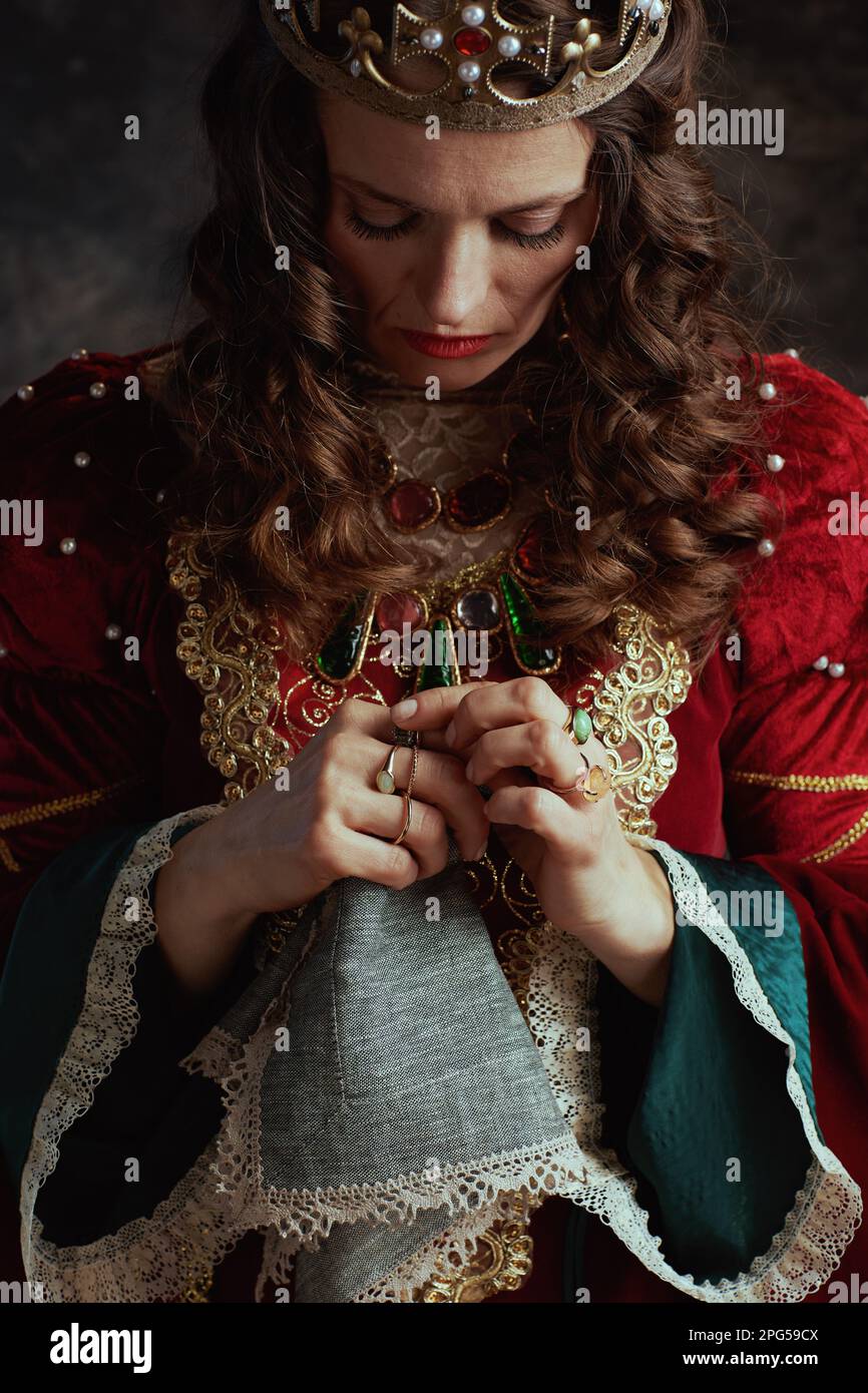 unhappy medieval queen in red dress with handkerchief and crown on dark ...