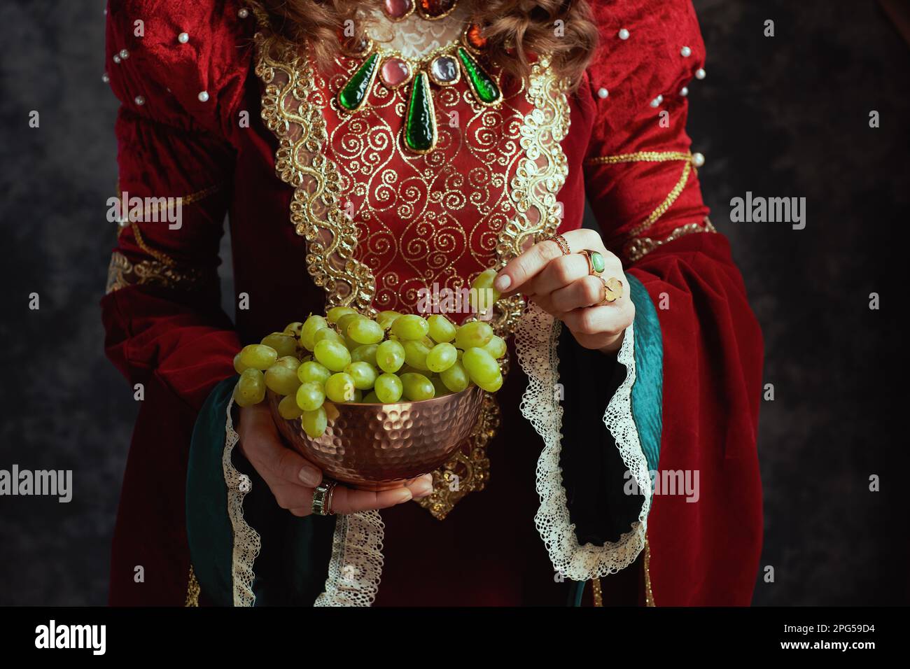 Closeup on medieval queen in red dress with plate of grapes on dark ...