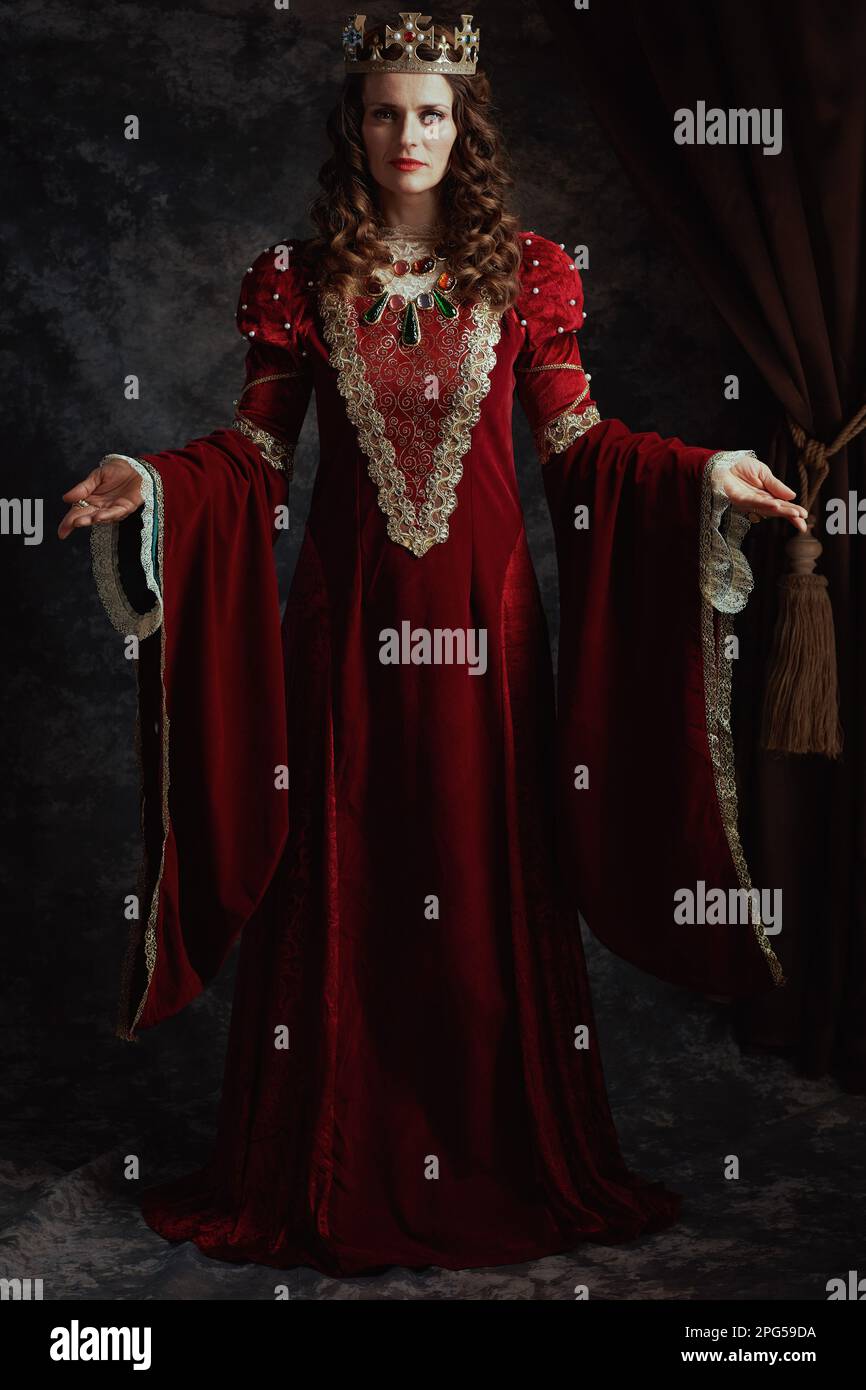 Full length portrait of medieval queen in red dress with crown on dark ...