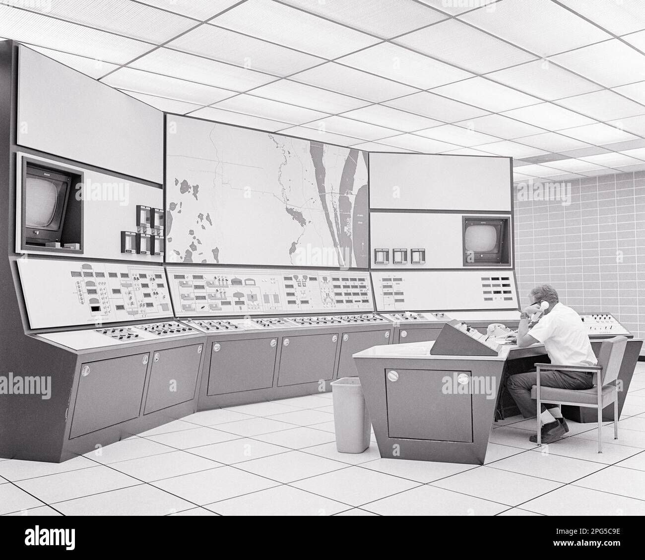 1970s MAN SITTING AT DESK CONSOLE ON TELEPHONE AT CONTROL PANELS OF A ...
