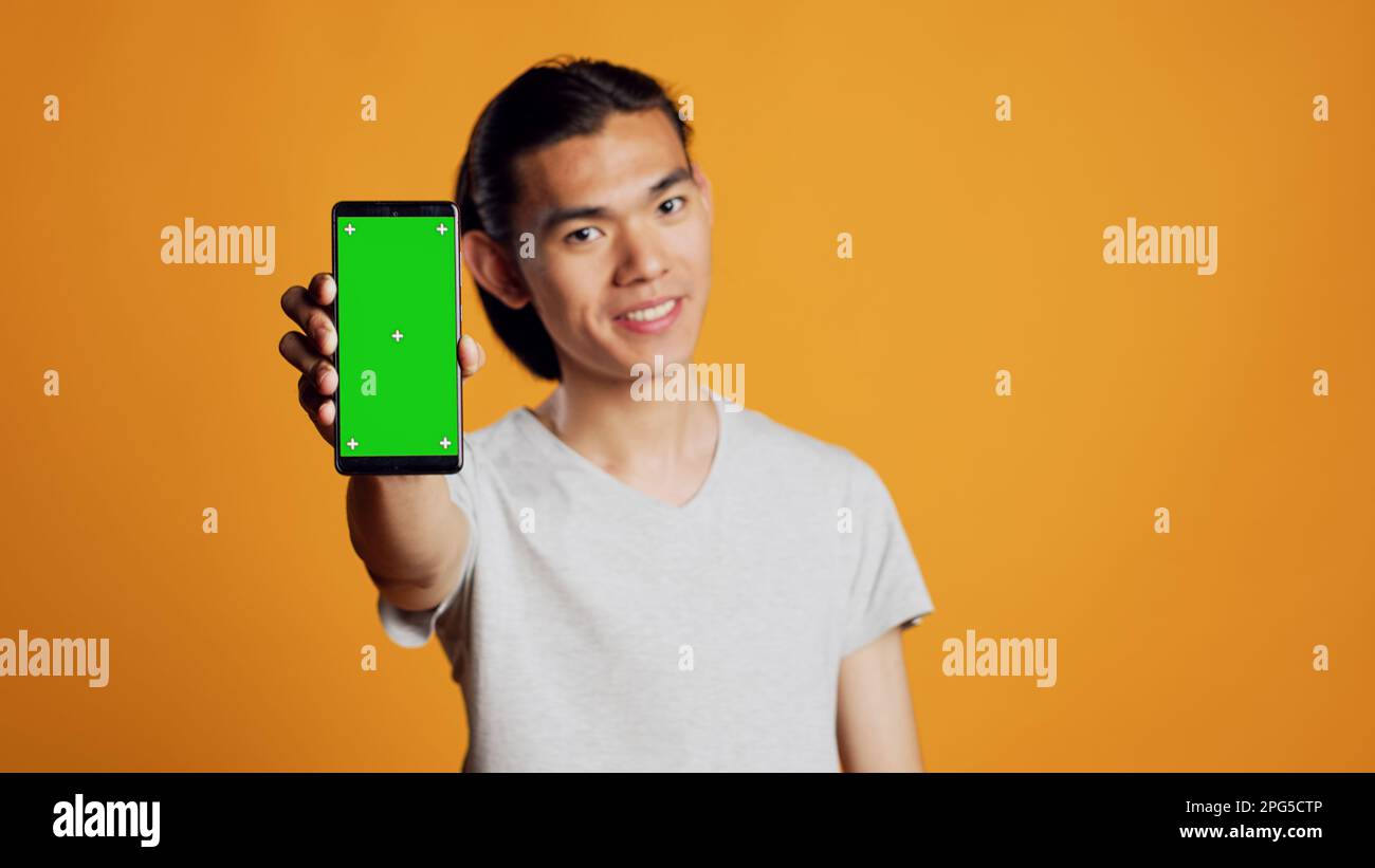 Cheerful young guy showing phone with greenscreen on camera, looking at ...