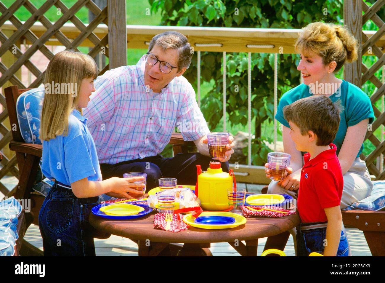 1990s SMILING FAMILY AT PICNIC TABLE ON BACK PATIO PORCH TALKING ...