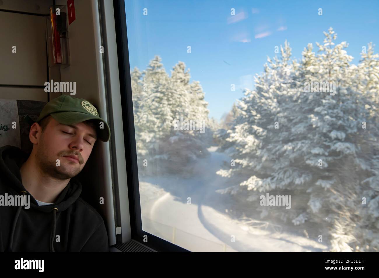 A man snoozes on a train in Norway with snow covered trees outside the ...