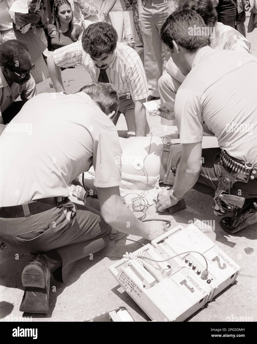 1970s EMTS POLICEMAN AND BYSTANDERS HELPING A MAN WHO HAD COLLAPSED ON ...