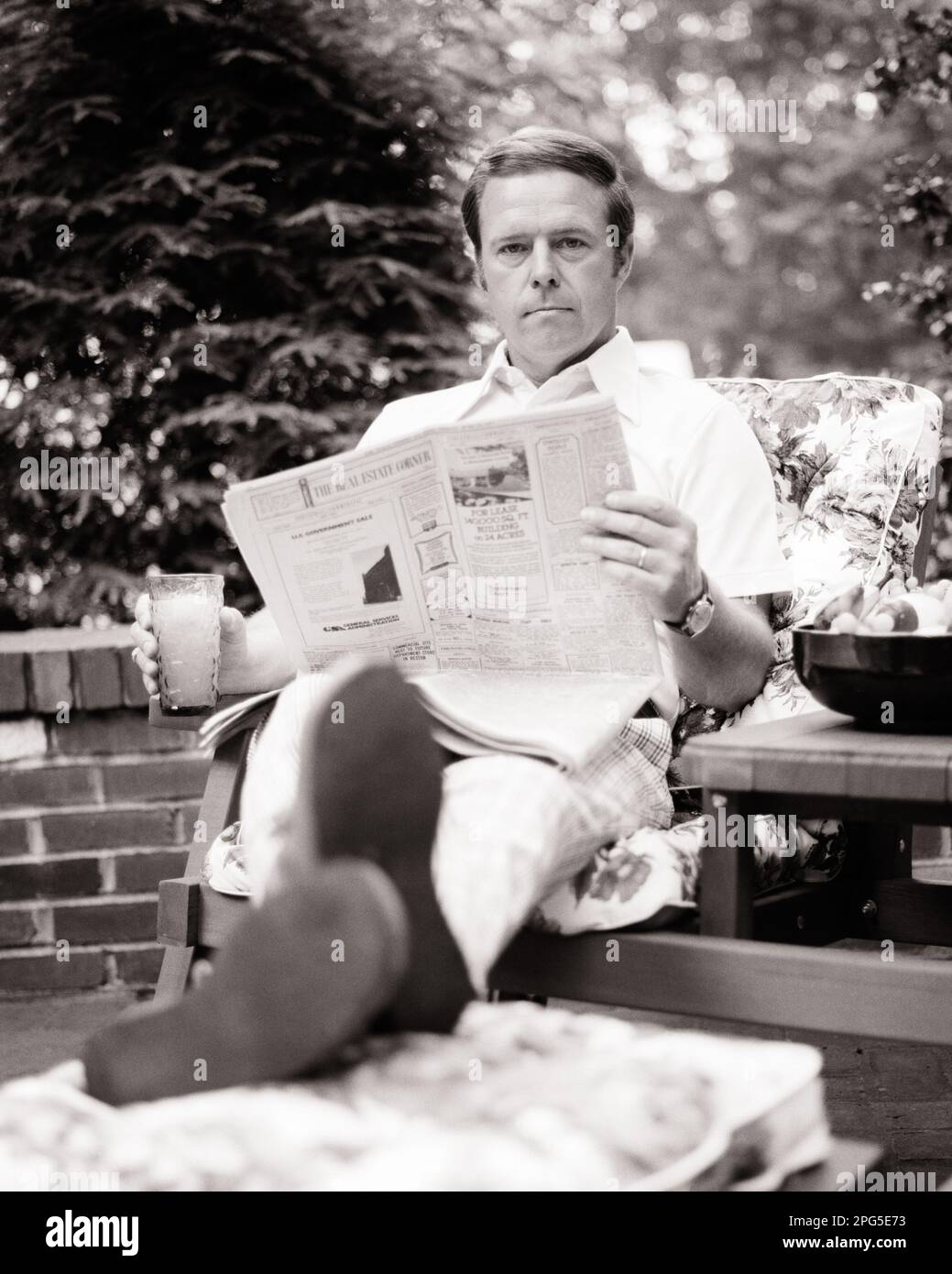 1970s MATURE MAN SITTING READING NEWSPAPER FEET UP OUTDOOR PATIO CHAIR ...