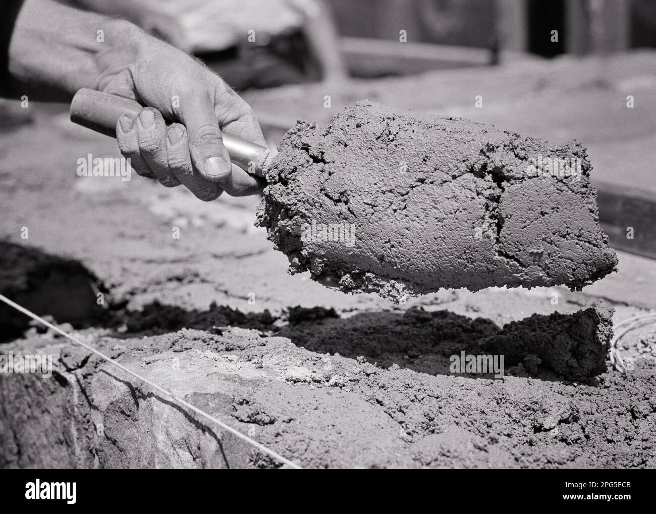 1950s HAND OF A MAN HOLDING A TROWEL FULL OF MORTAR CEMENT BUILDING A ...