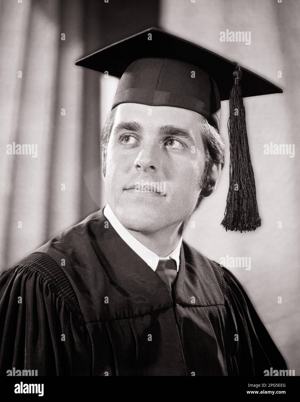 1970s COLLEGE GRADUATE WEARING CAP AND GOWN LOOKING OFF TO THE LEFT ...