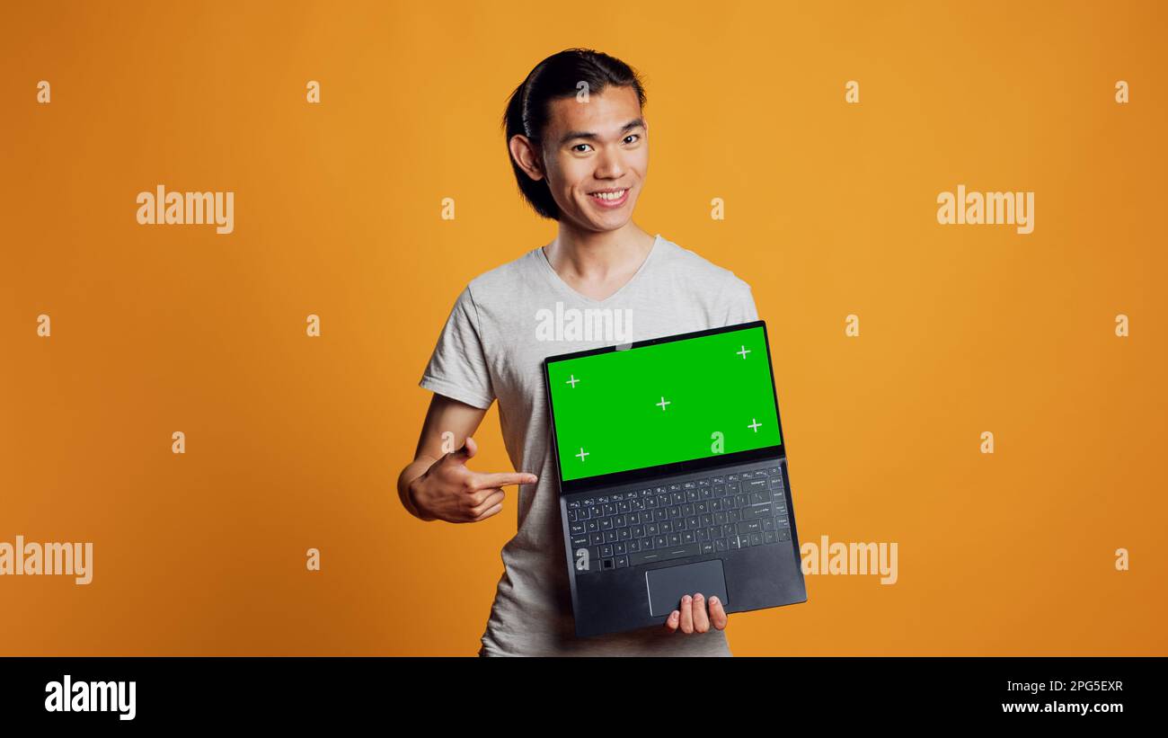 Cheerful man holding laptop with greenscreen on camera, showing ...