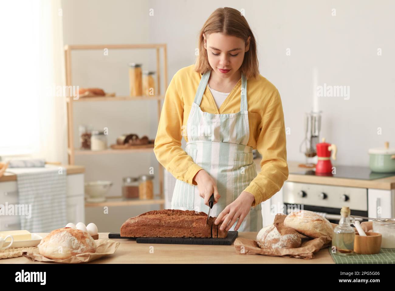Female baker cutting rye bread at table in kitchen Stock Photo - Alamy