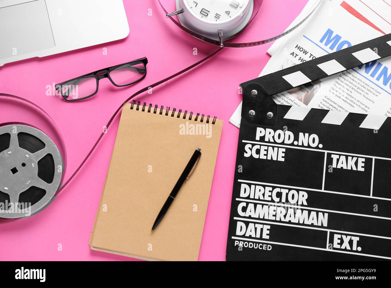 Notebook with movie clapper, film reel and newspapers on pink ...