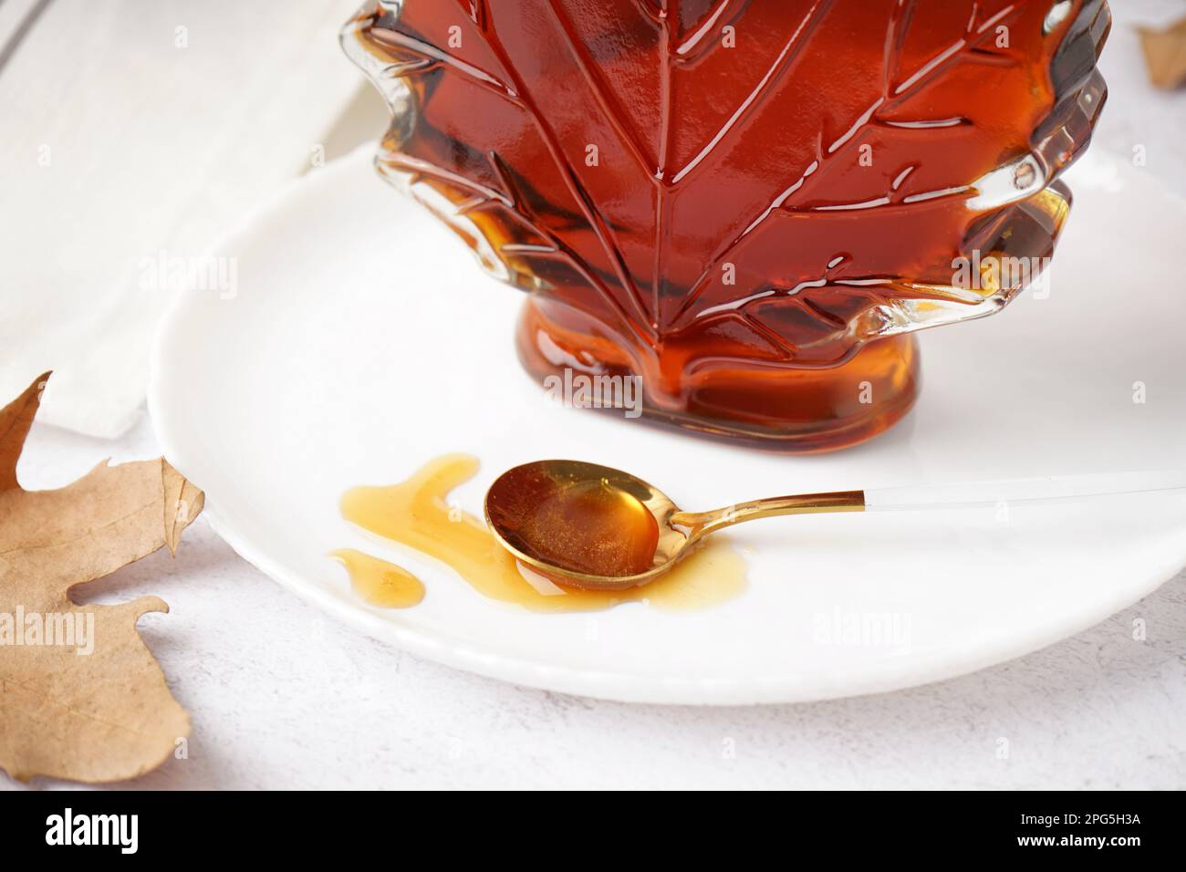 Bottle and spoon of spilled tasty maple syrup on white table Stock ...