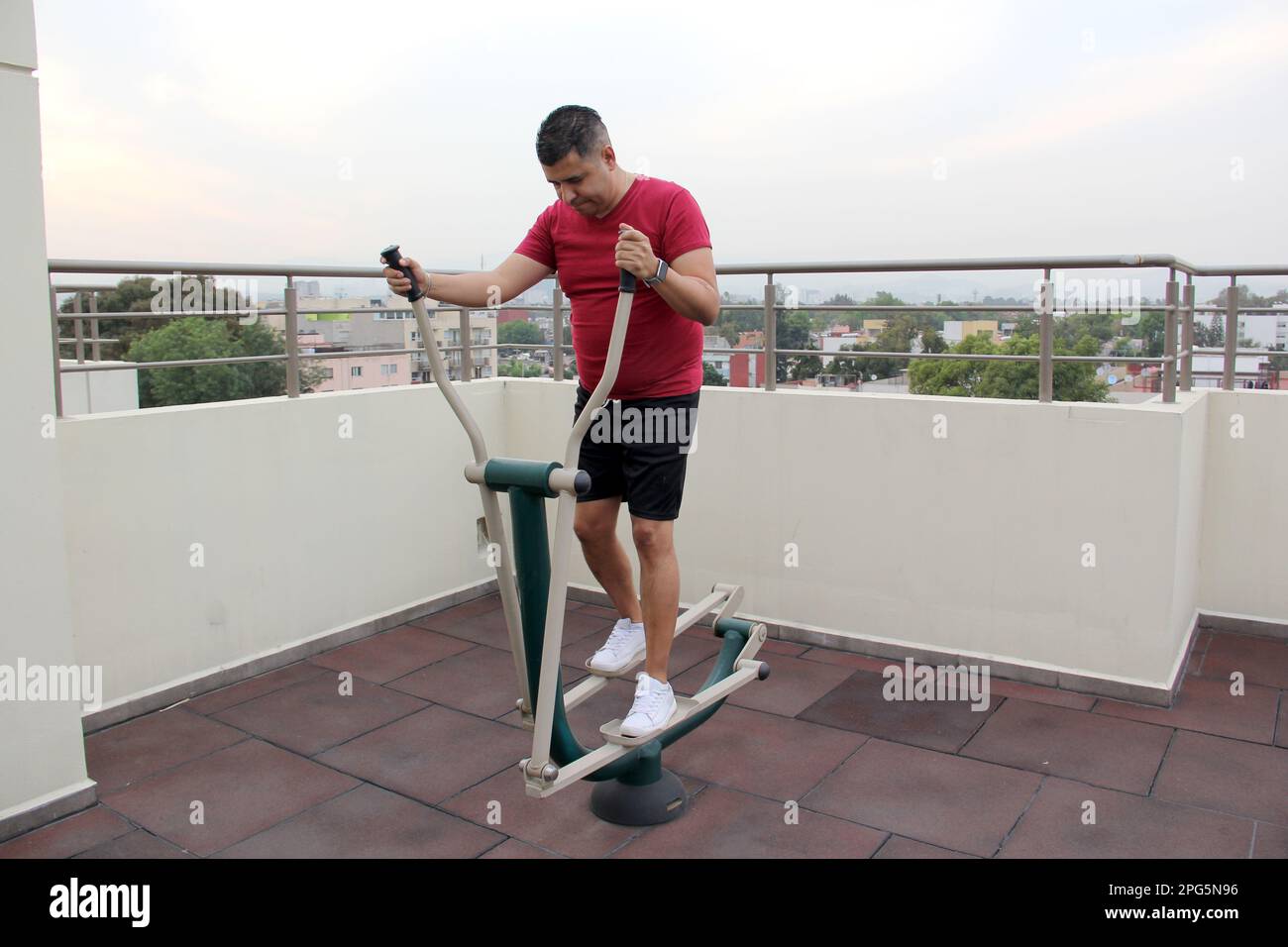 Adult 40-year-old Latino man exercises on the roof garden of her apartment with shared public ...